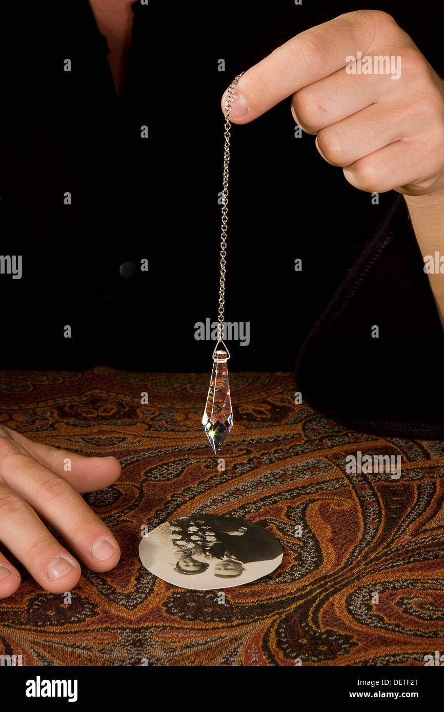 Hand holding a tarot pendulum above a photo of a deceased couple (the ...
