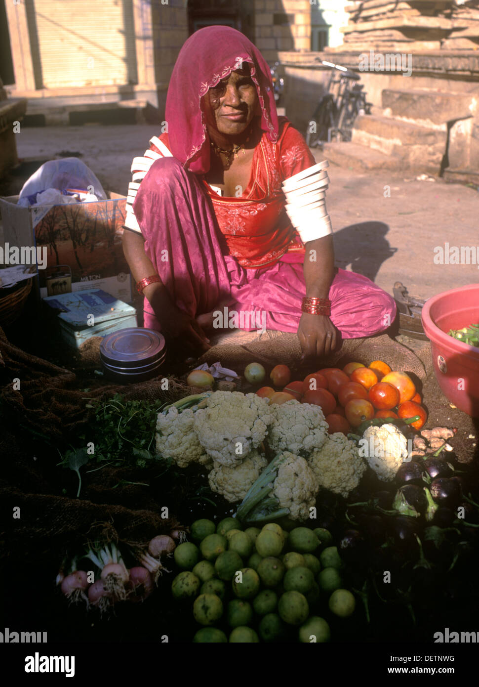Woman in colourful clothing squatting in street, selling fruit and vegetables. Pushkar in India ...