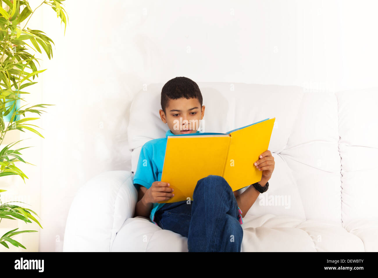 Beautiful black boy sitting with book reading on the coach with nice ...