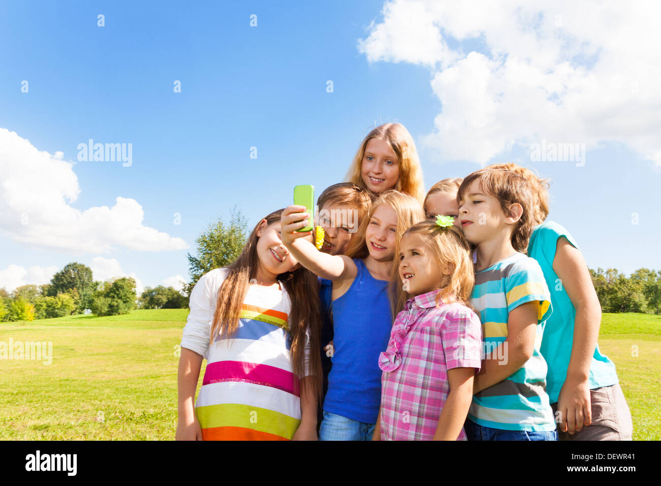 Group of happy kids taking picture of friends with smartphone standing ...