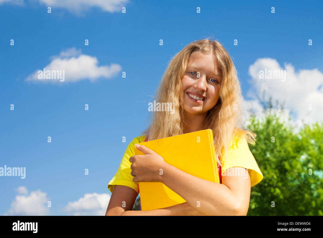 Happy blond 13 years old girl stand with with the yellow book in the ...