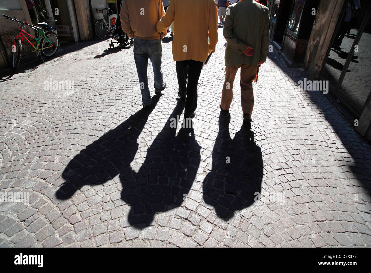The shadows of three elderly men walking down a cobbled street in ...
