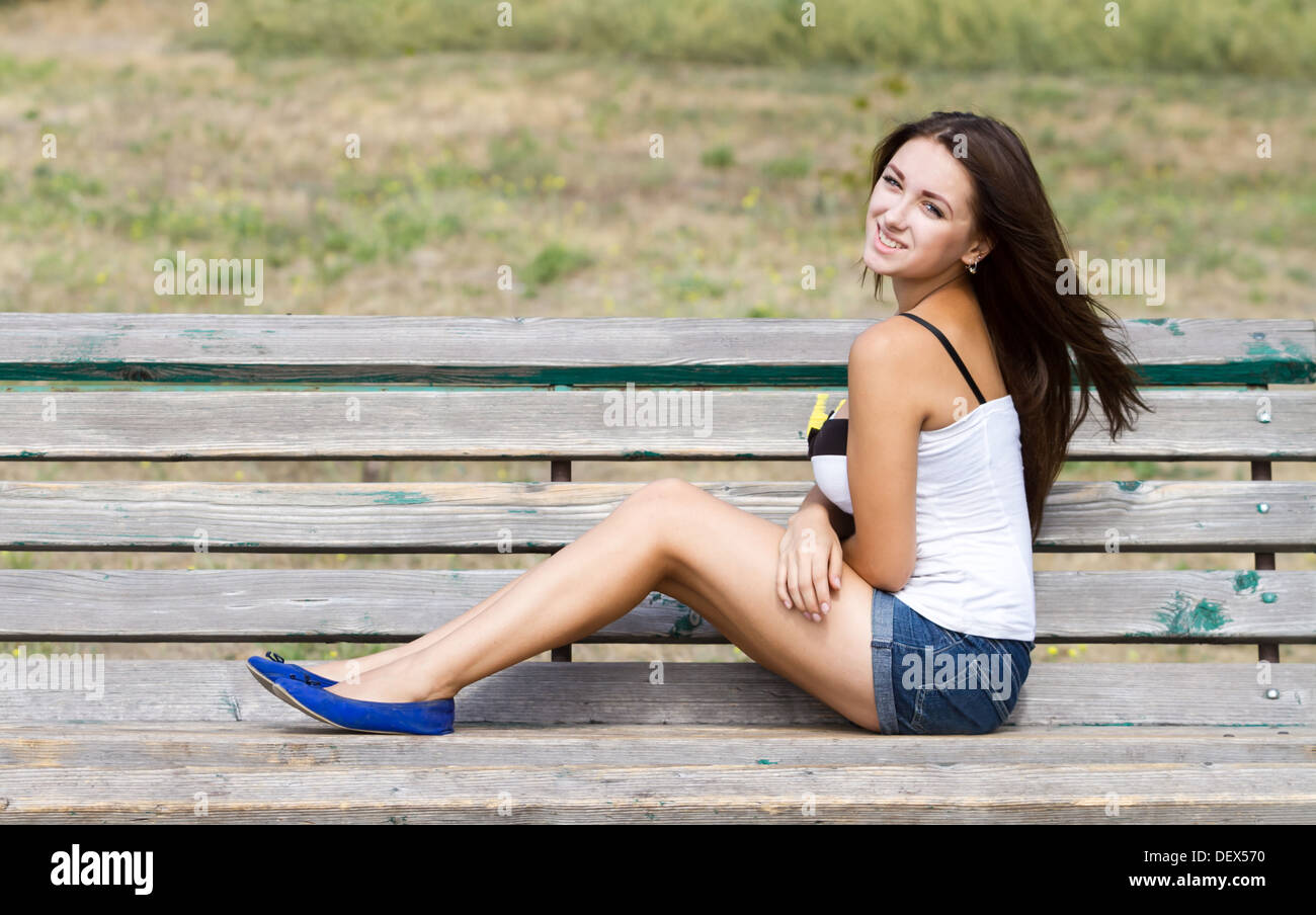 Happy young girl sitting on a bench in a summer day. Shot with lots of ...