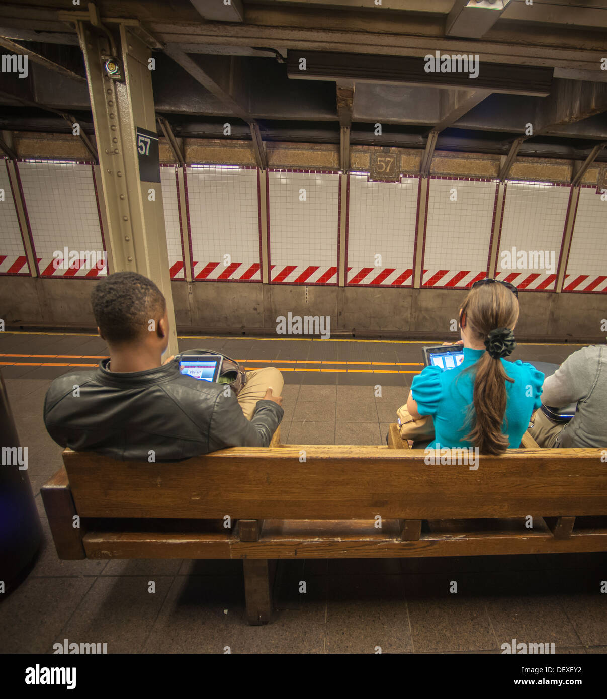 Subway riders use their tablet computers on a subway platform while ...