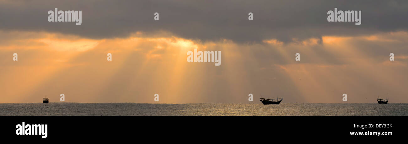 Sun beams above the Arabian Sea with the silhouettes of typical dhows ...