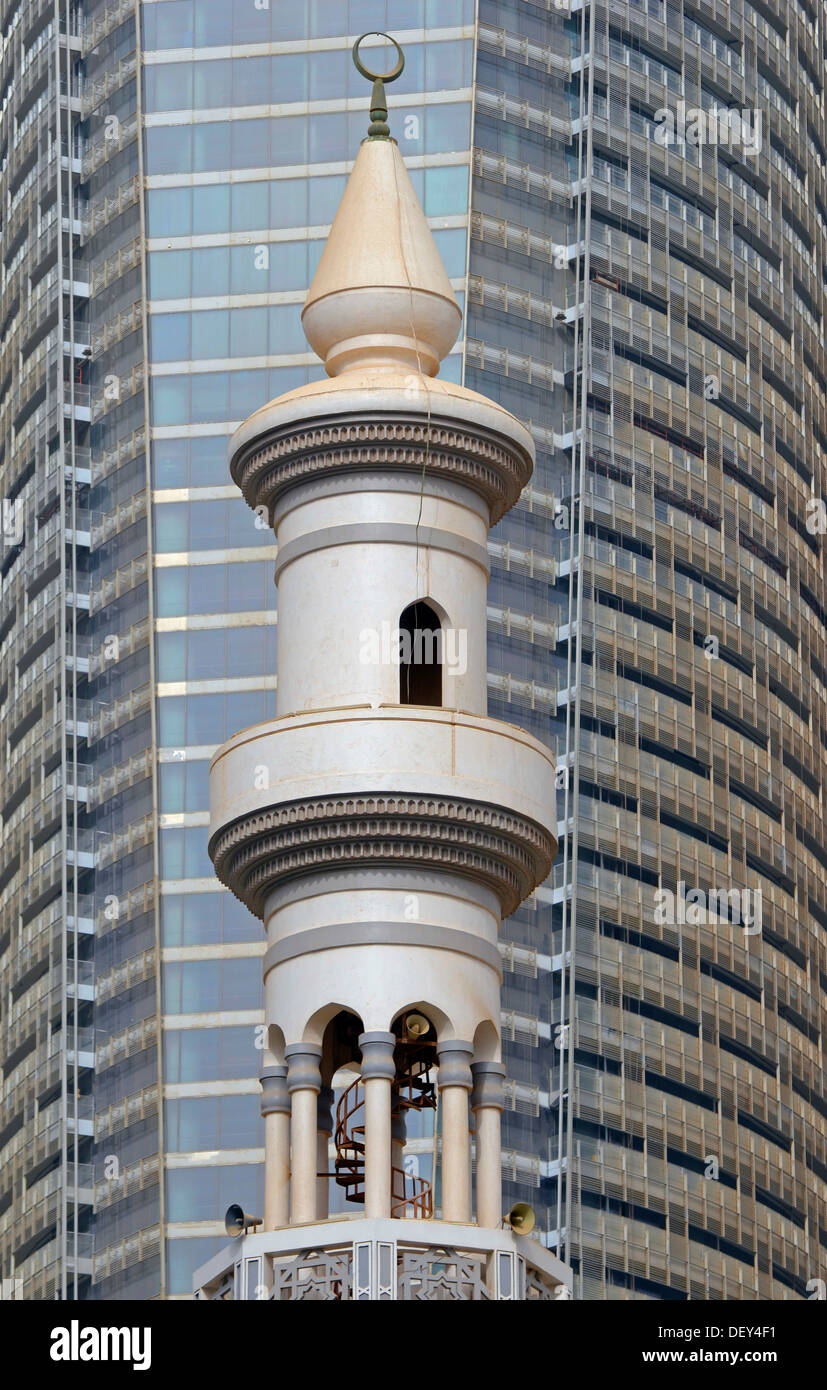 The minaret of a small mosque against the modern glass and steel facade ...