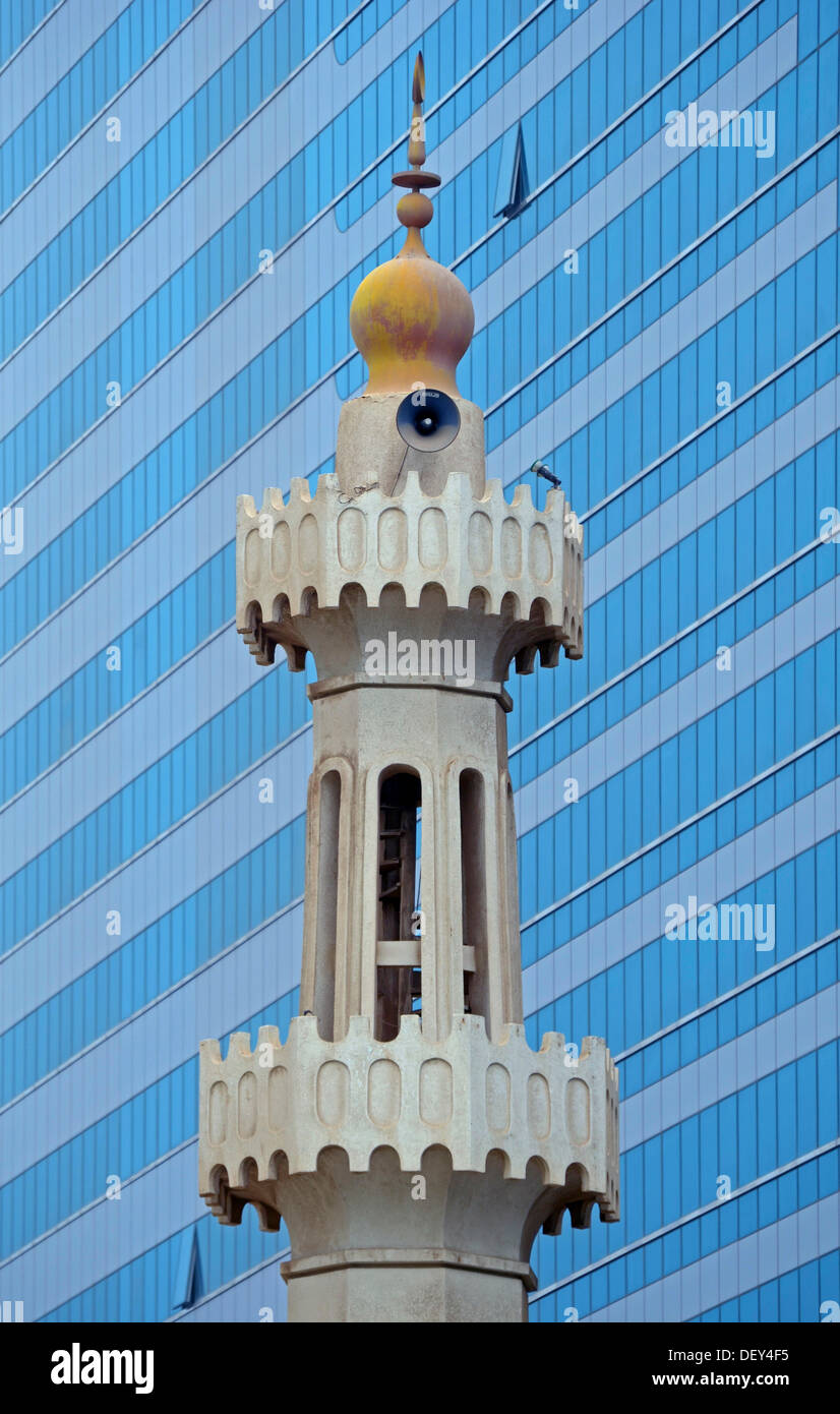 The minaret of a small mosque against the modern glass and steel facade ...