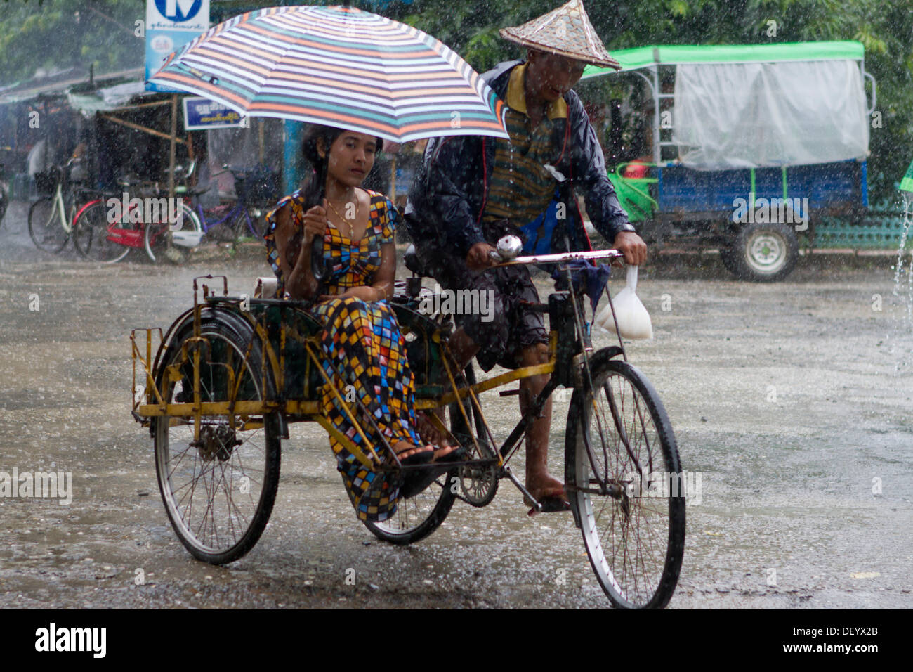 A woman rides a tricycle rickshaw in the rain along the Main Road in ...