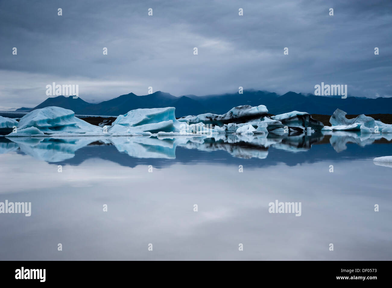 Blue and black ash-coloured icebergs, reflected in the glacier lagoon ...