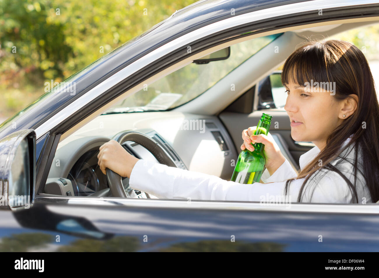 Happy inebriated female driver holding a botttle of alcohol and smiling ...