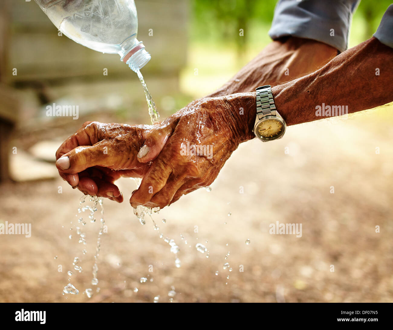 Old man washing his hands with water pouring from a plastic bottle ...