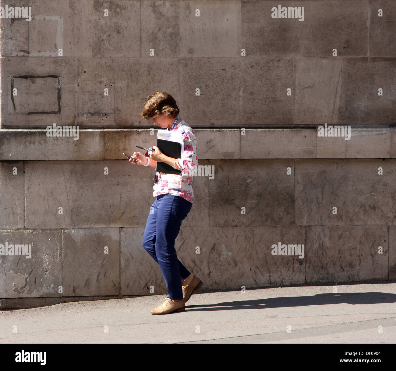 Young woman with her cell phone, texting whilst walking in an old part ...