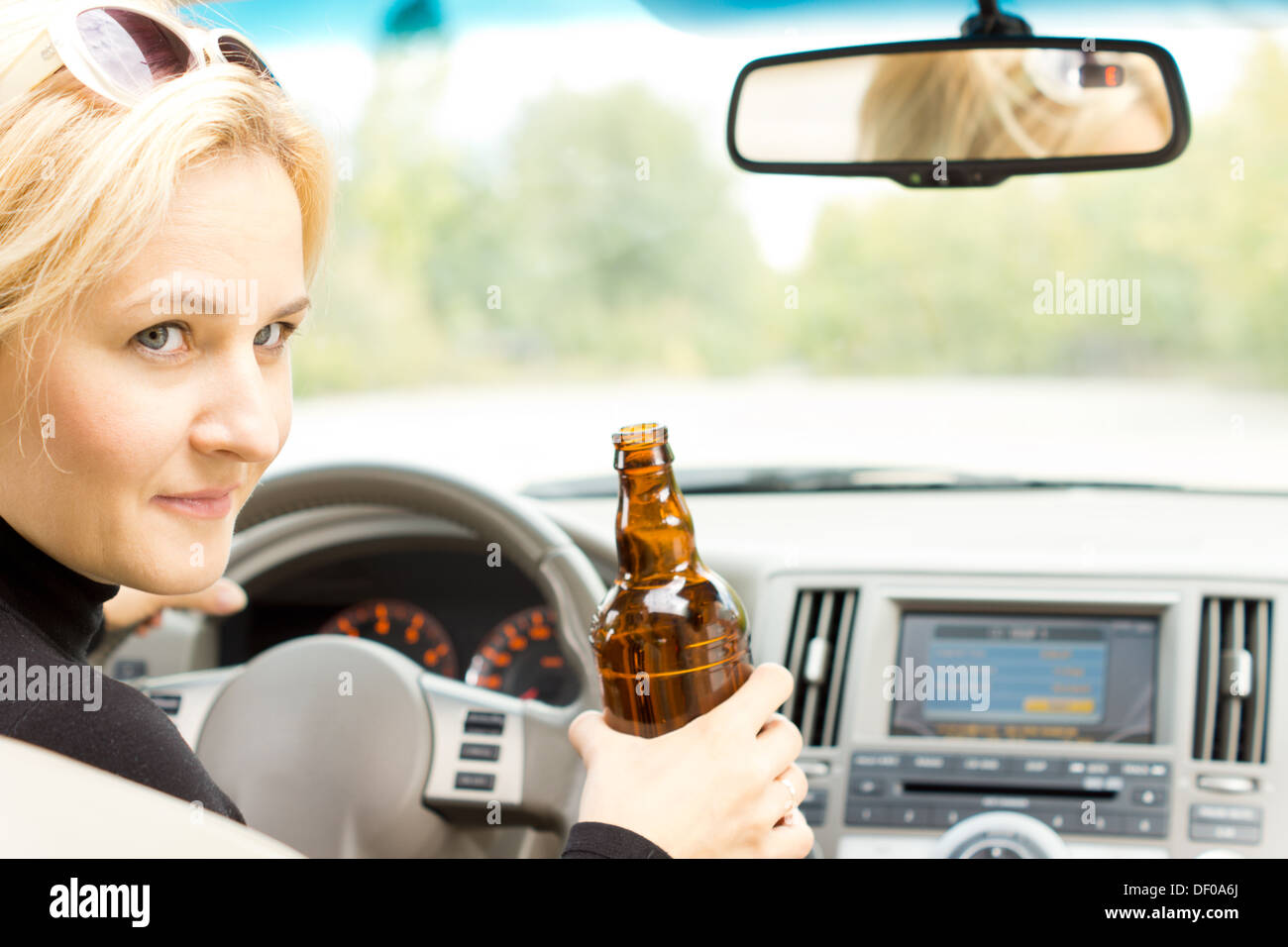 Smiling female driver drinking alcohol from a bottle and turning to the ...