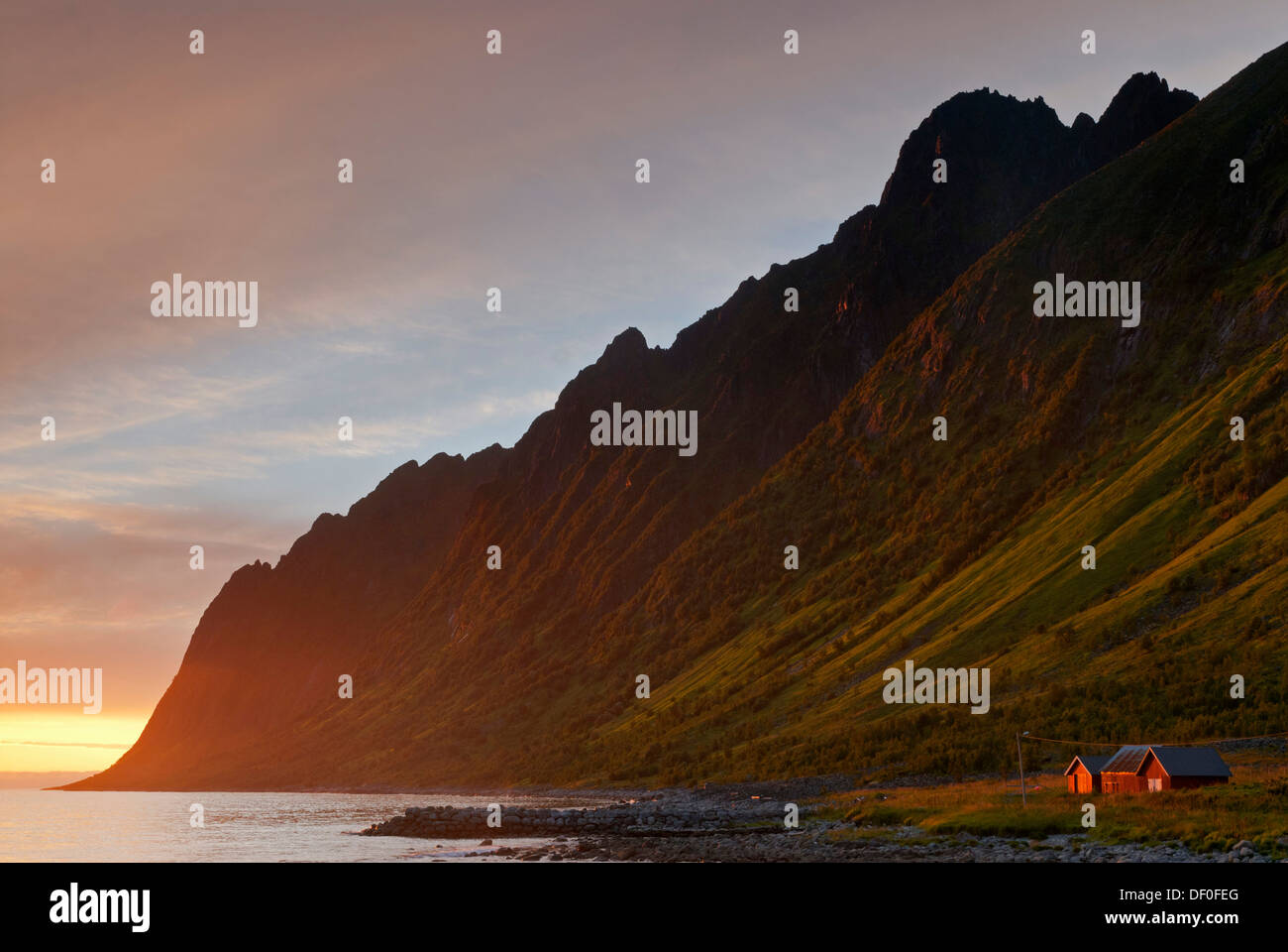 Sun set over the Norwegian Sea behind typical red Rorbuer huts, rorbu ...
