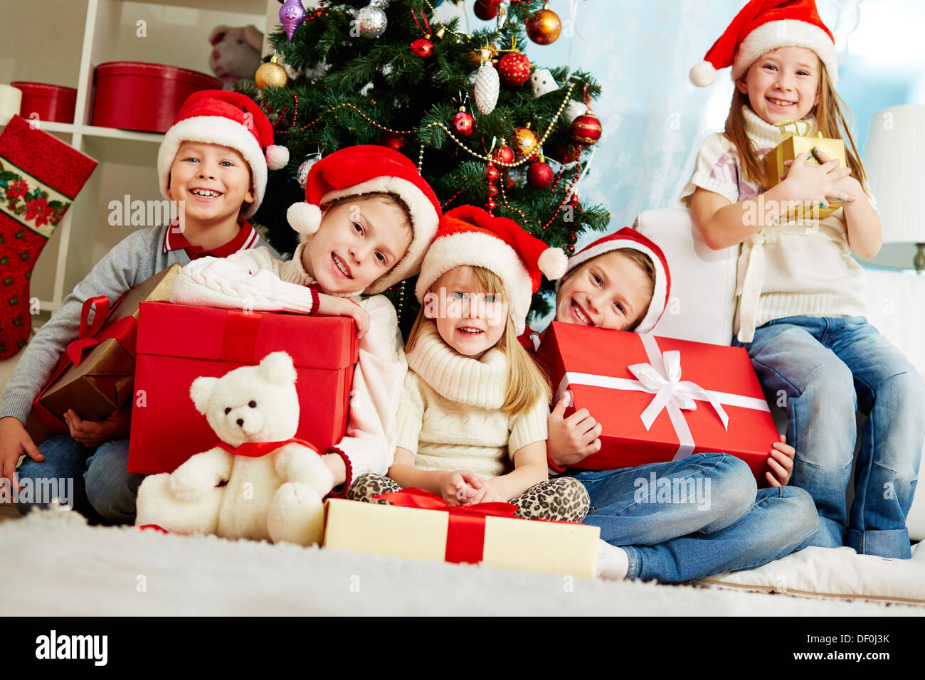 Group of adorable kids in Santa caps looking at camera while sitting by ...