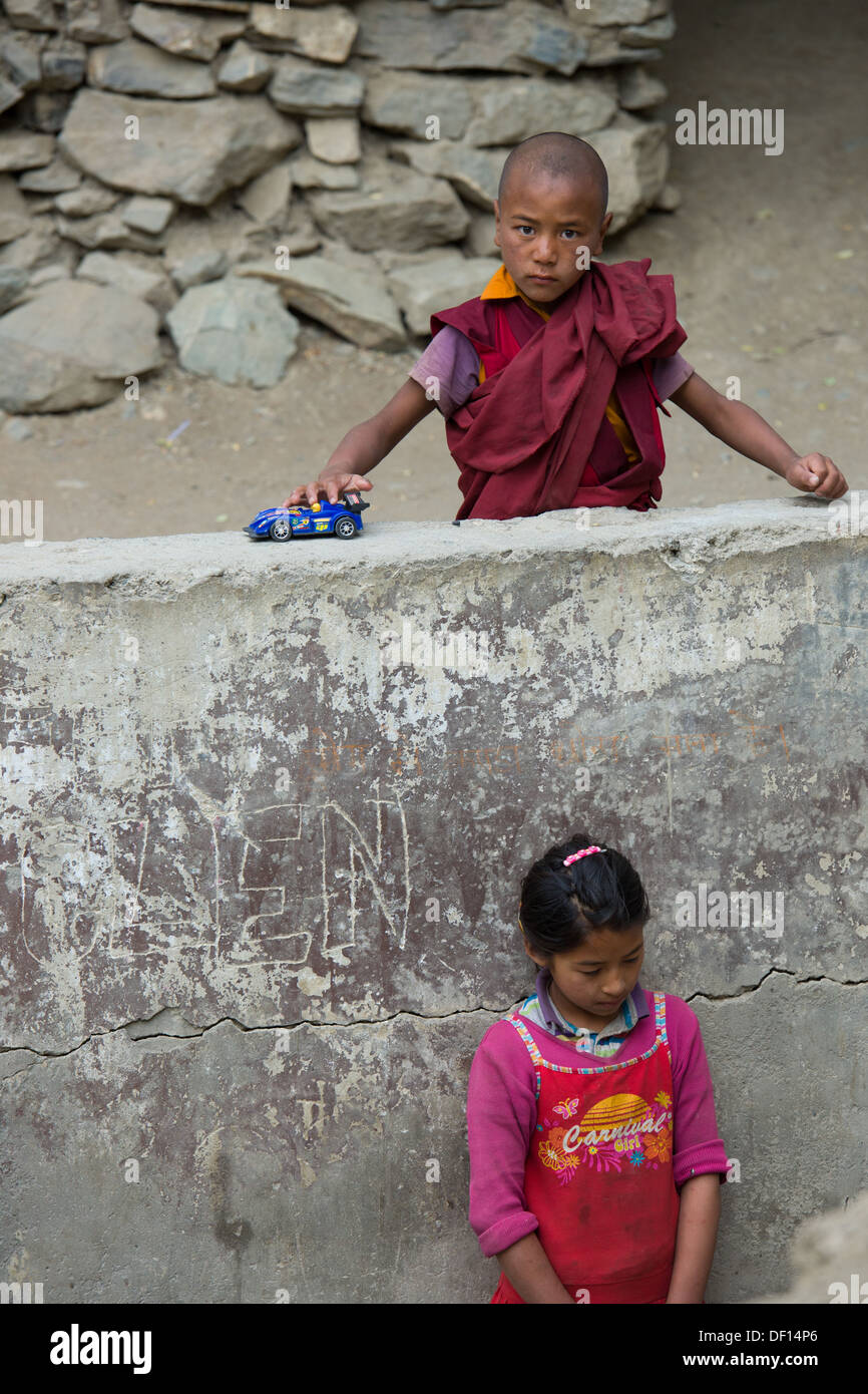 Novice monk playing with a toy racing car above a young girl, Lamayuru ...
