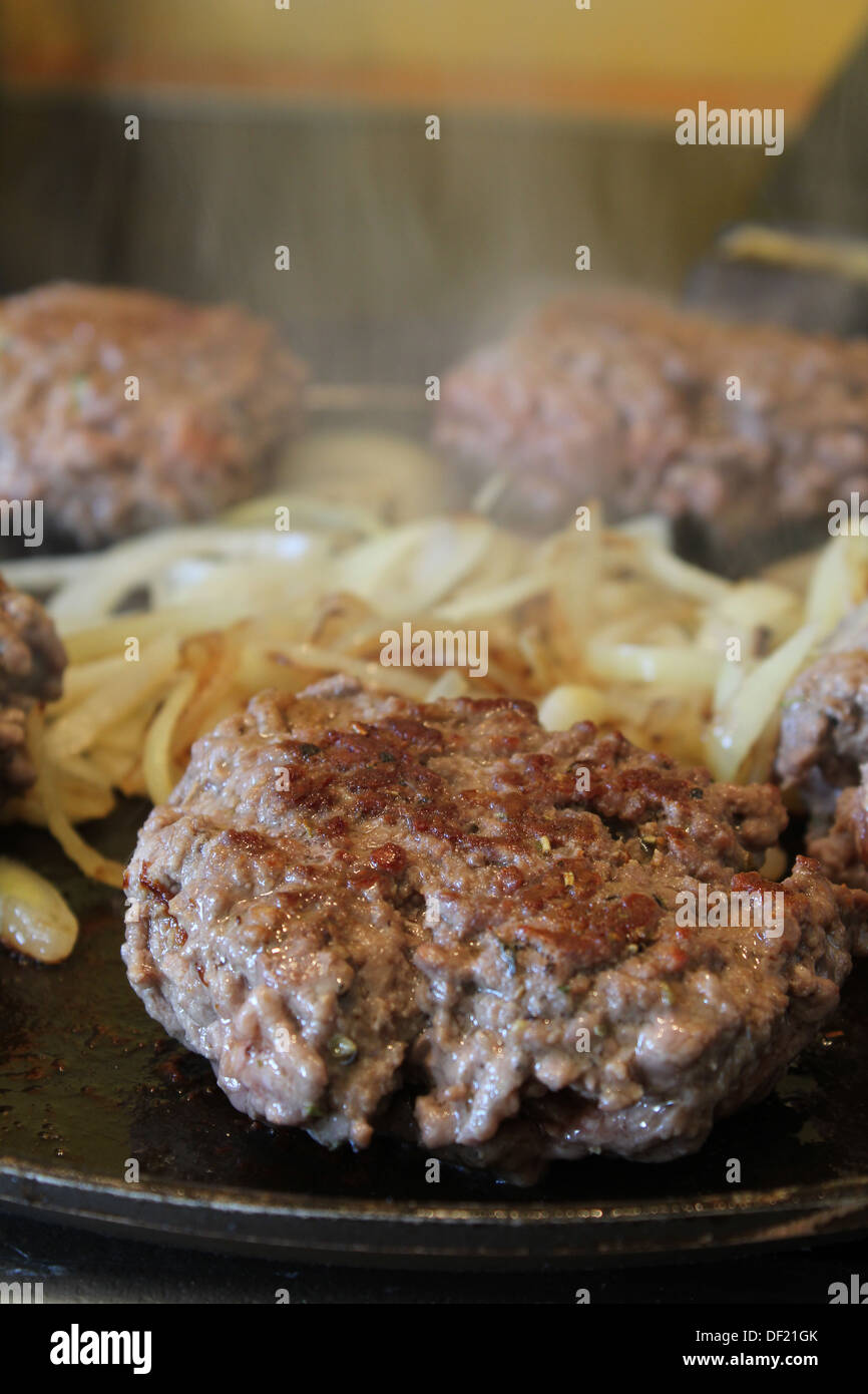Burger sizzling with onions in frying pan Stock Photo - Alamy