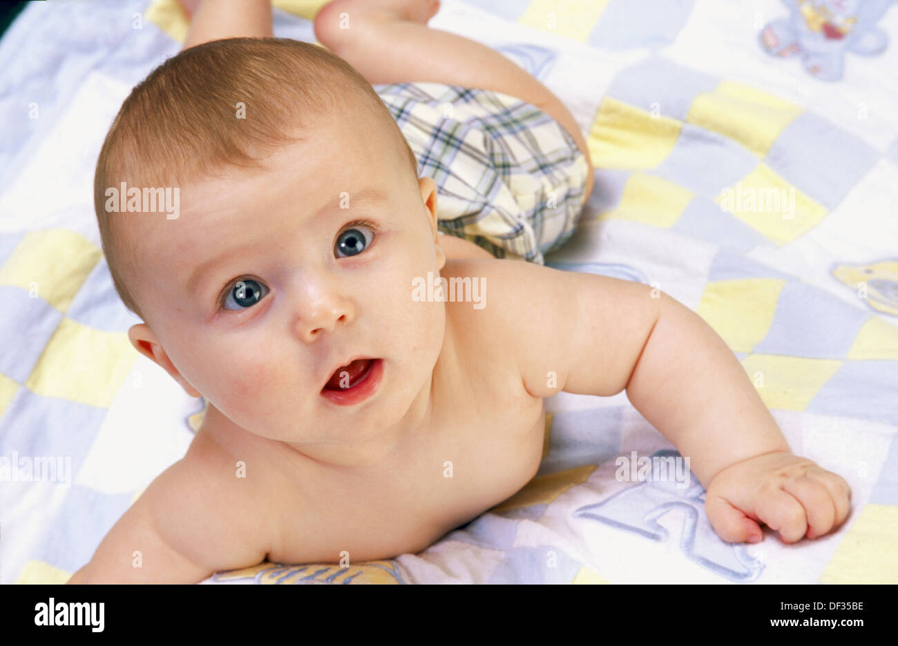 Baby boy almost rolls over onto back while laying on quilt Stock Photo ...