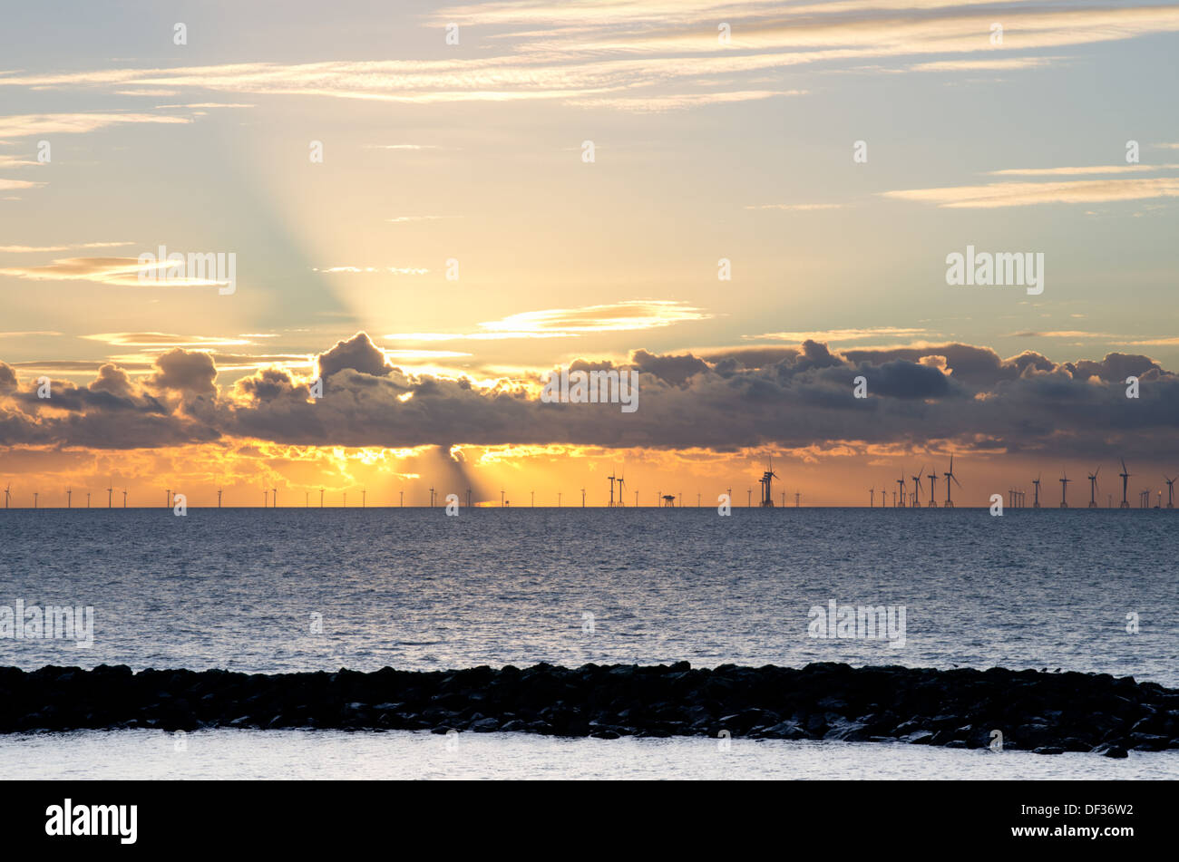 A sunset over an offshore wind farm with the sun hidden behind a thin ...