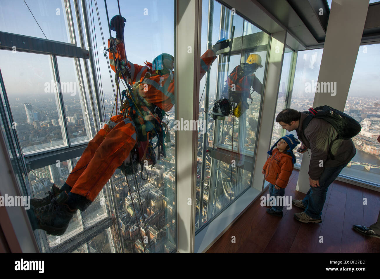 Child looking at abseiling window-cleaners cleaning the outside of the ...