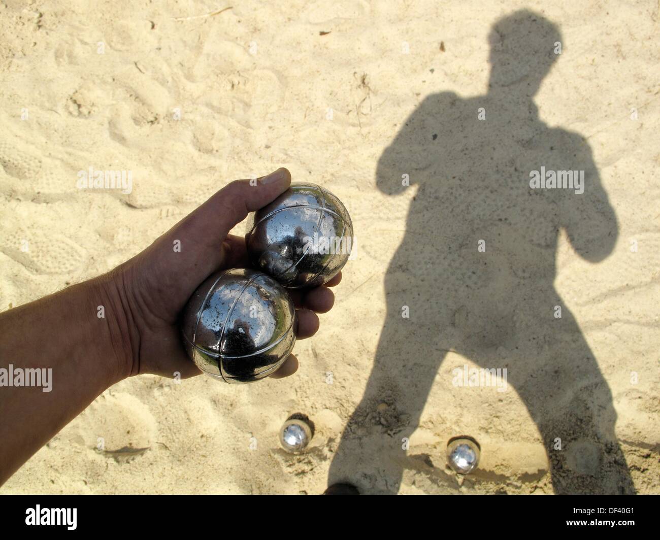 A man holding two bocce balls in his hand, his shadow in the background ...