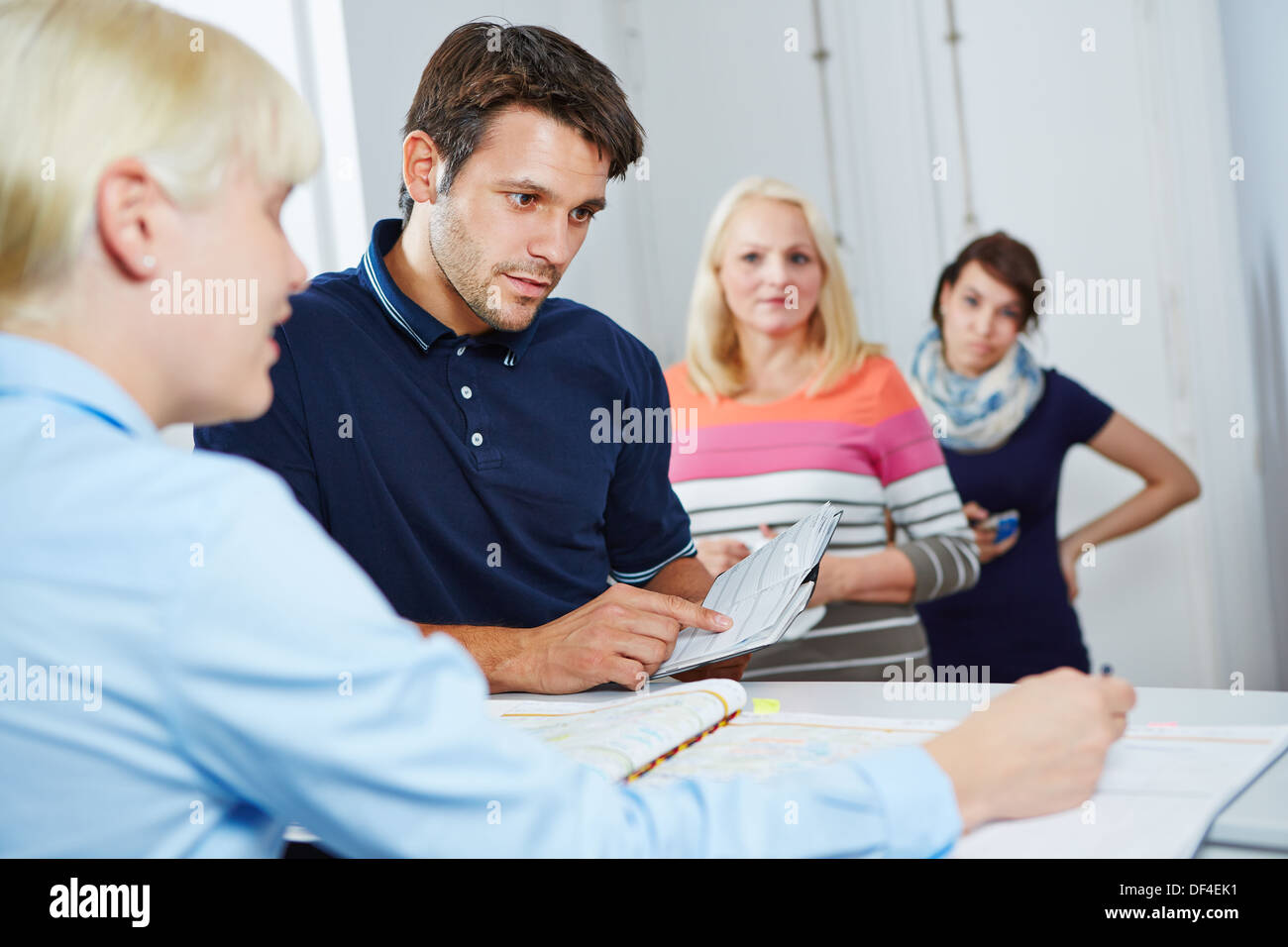 Man scheduling appointment with doctors assistant while people waiting ...