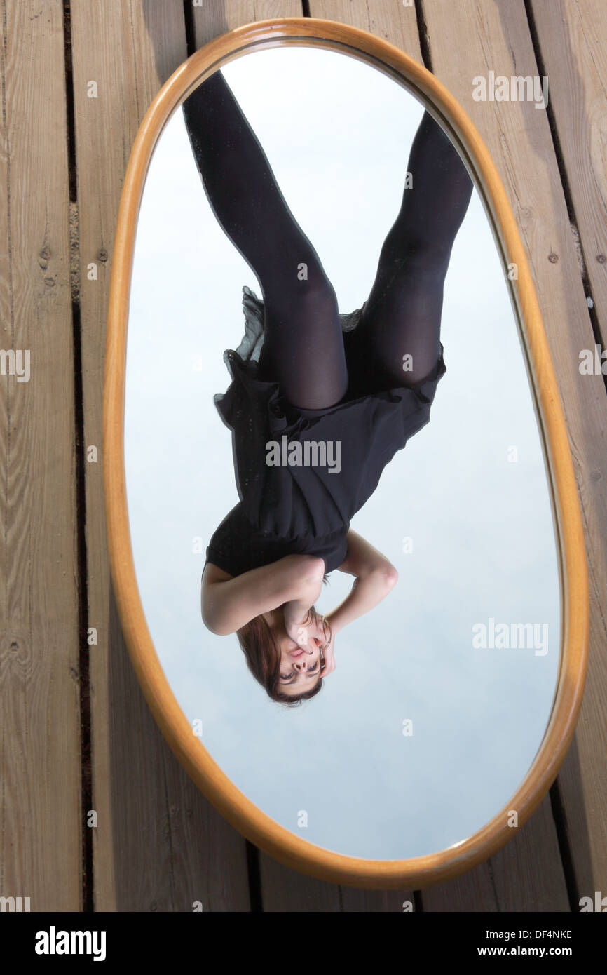 thoughtful young woman in black with her reflection in mirror ...