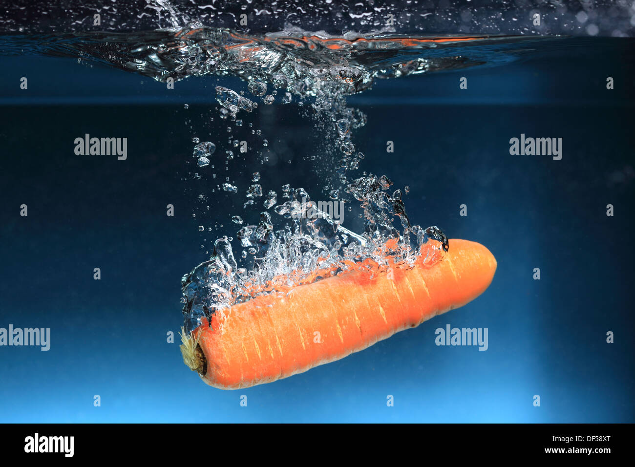 Carrot in the water splash over blue background. Healthy food and ...