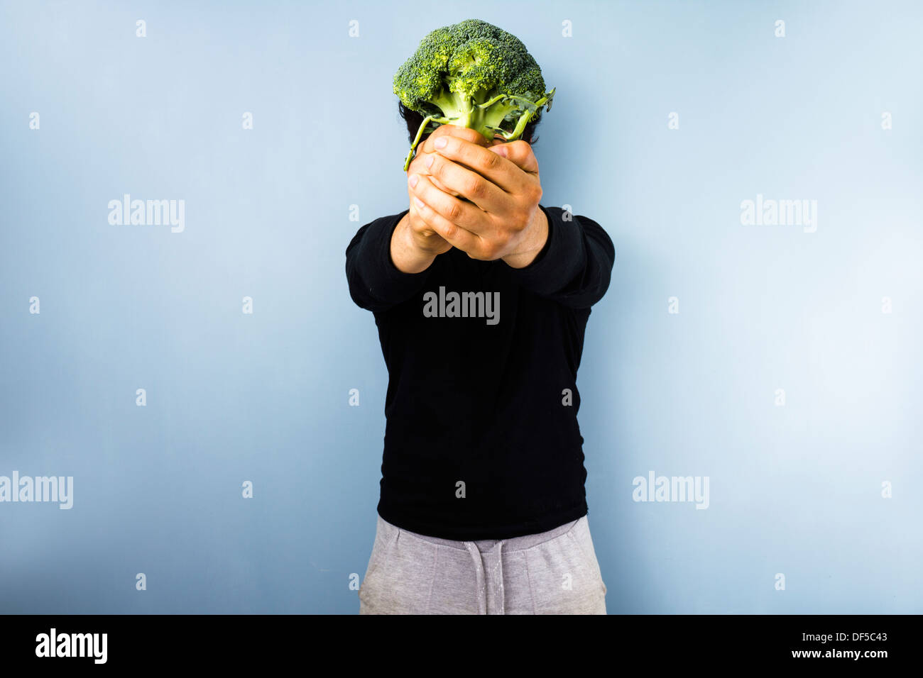 Young man holding a head of broccoli that's obscuring his face Stock ...