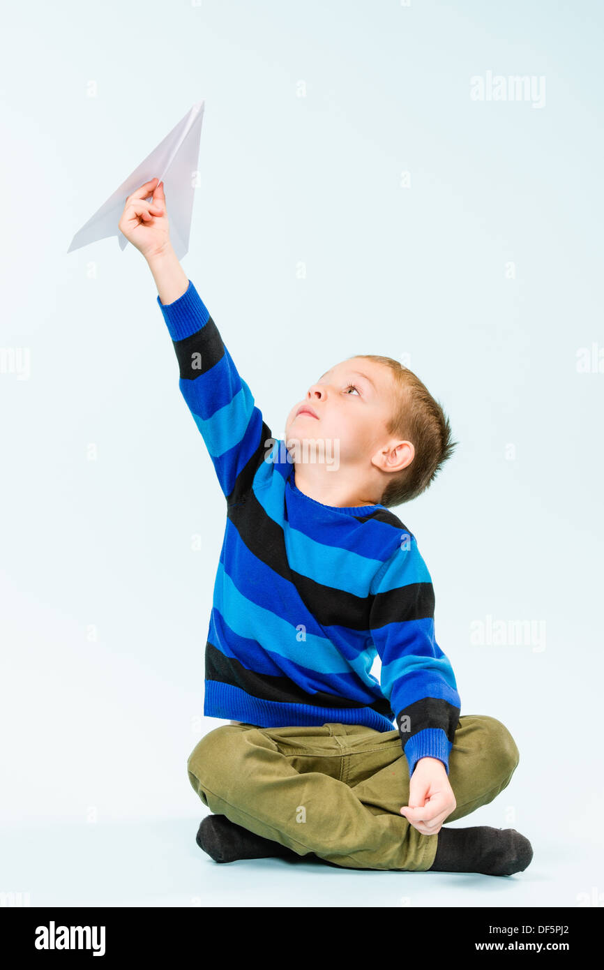 Happy boy playing with paper airplane in studio, light blue background ...