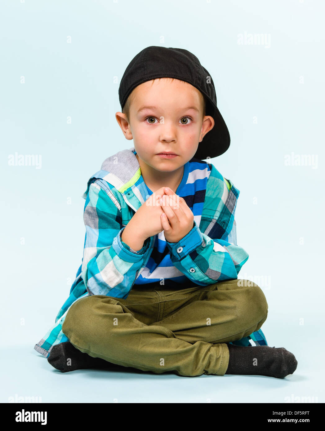 Surprised little boy wearing peaked cap on studio, light blue ...