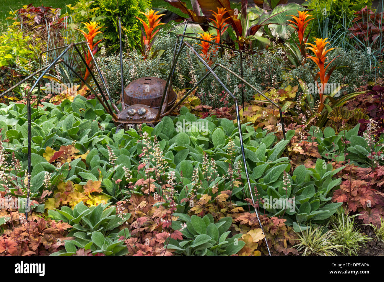 Rusty metal spider decorating a garden with colorful variety of plants ...