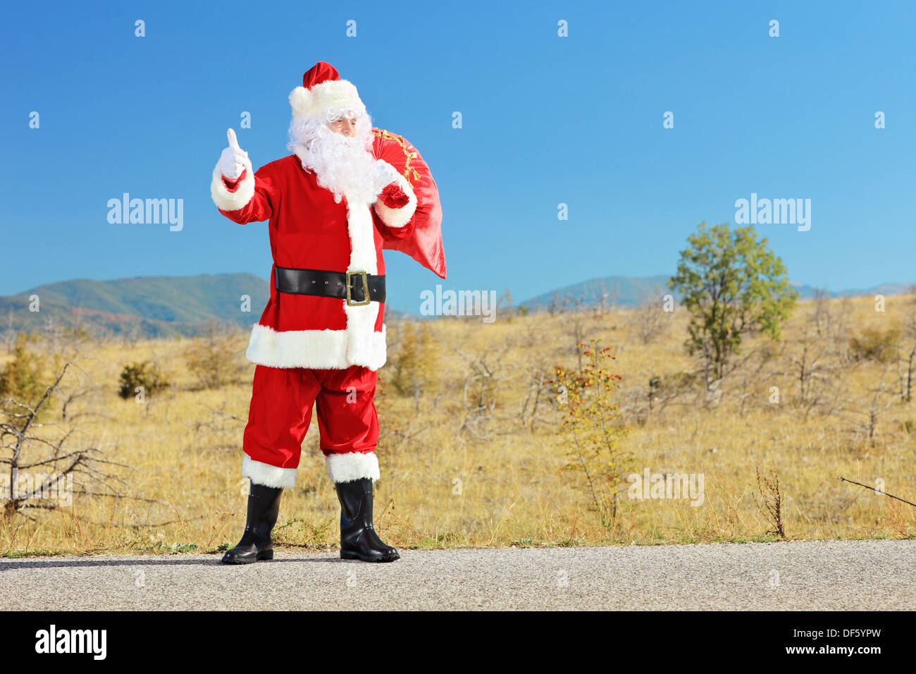 Full length portrait of a santa claus with bag hitchhiking on an open ...