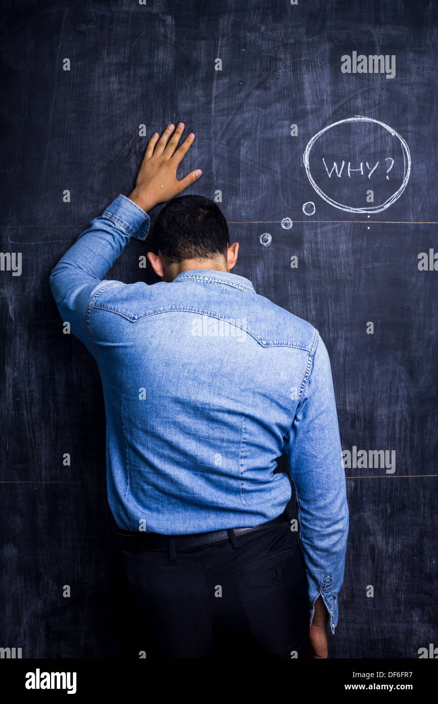 Sad young man is standing by a blackboard and asking himself why Stock ...