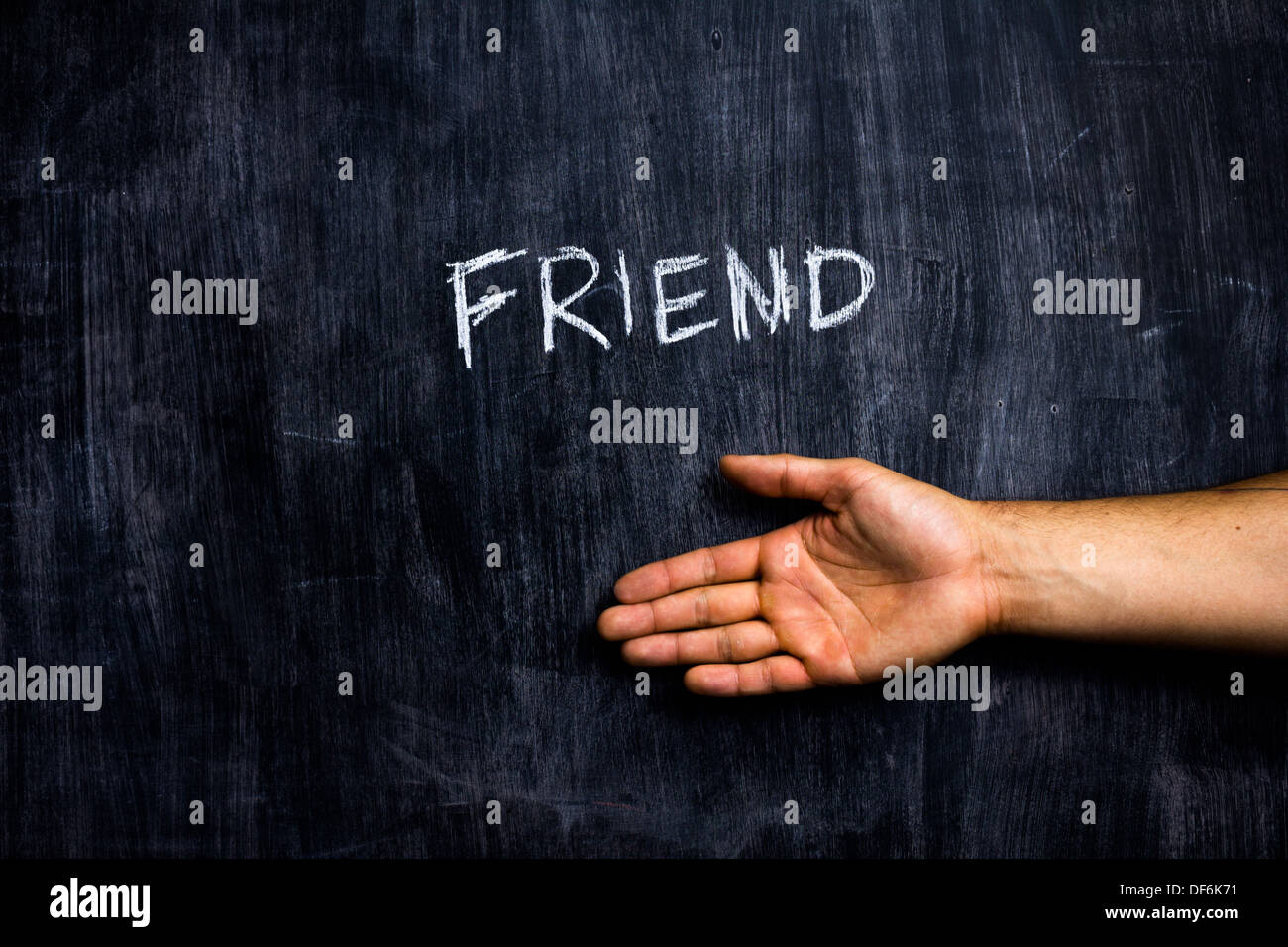 Hand offering handshake beneath the word friend written on blackboard ...