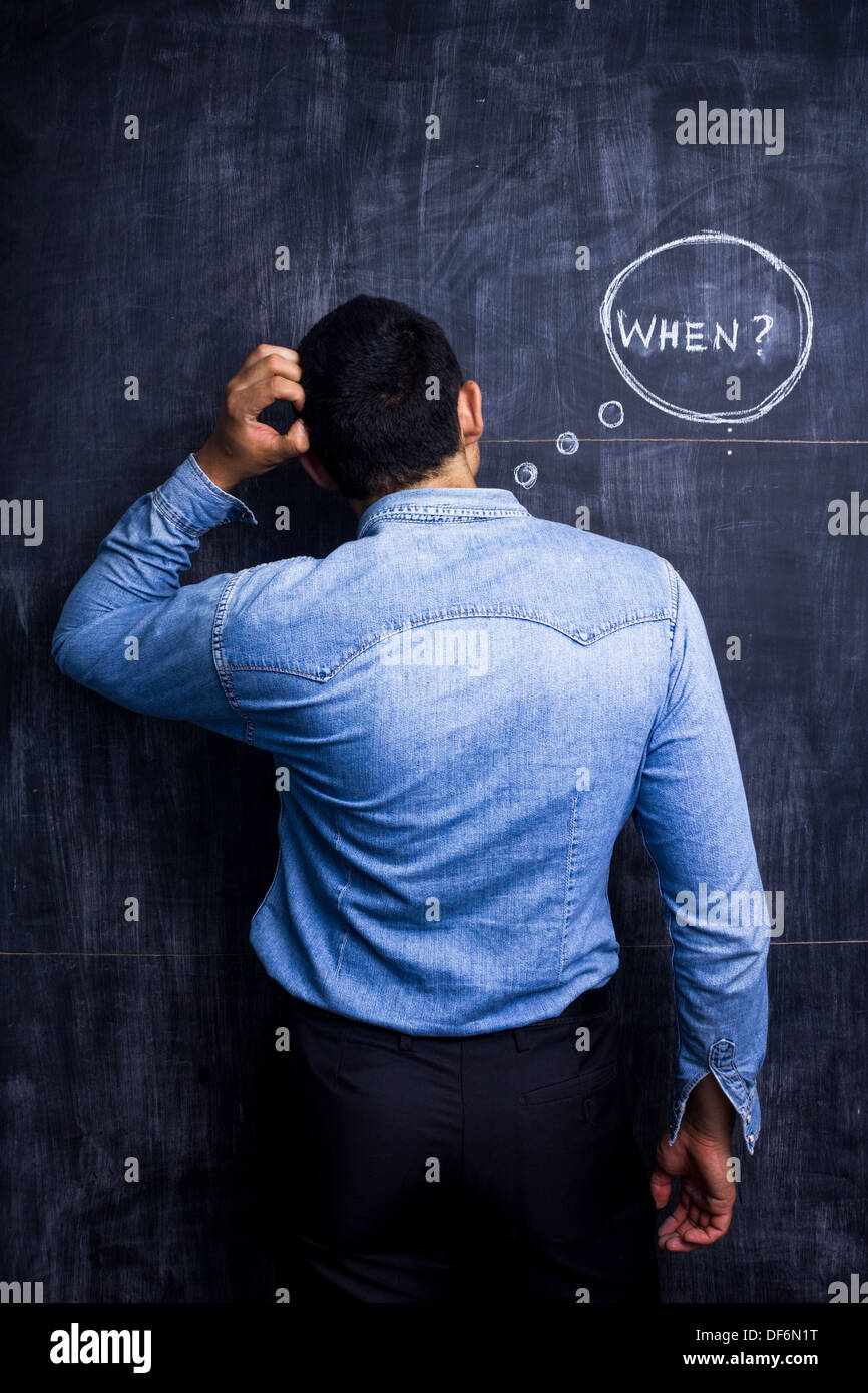 Rear view shot of a confused young man by blackboard asking when Stock ...
