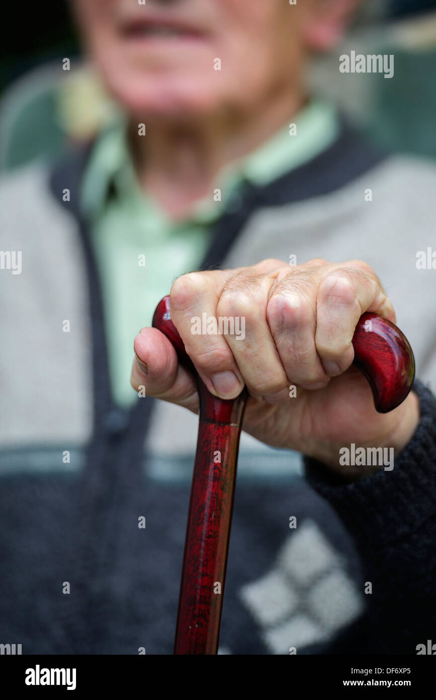 An elderly old age pensioner sits with his hands on a walking stick in ...