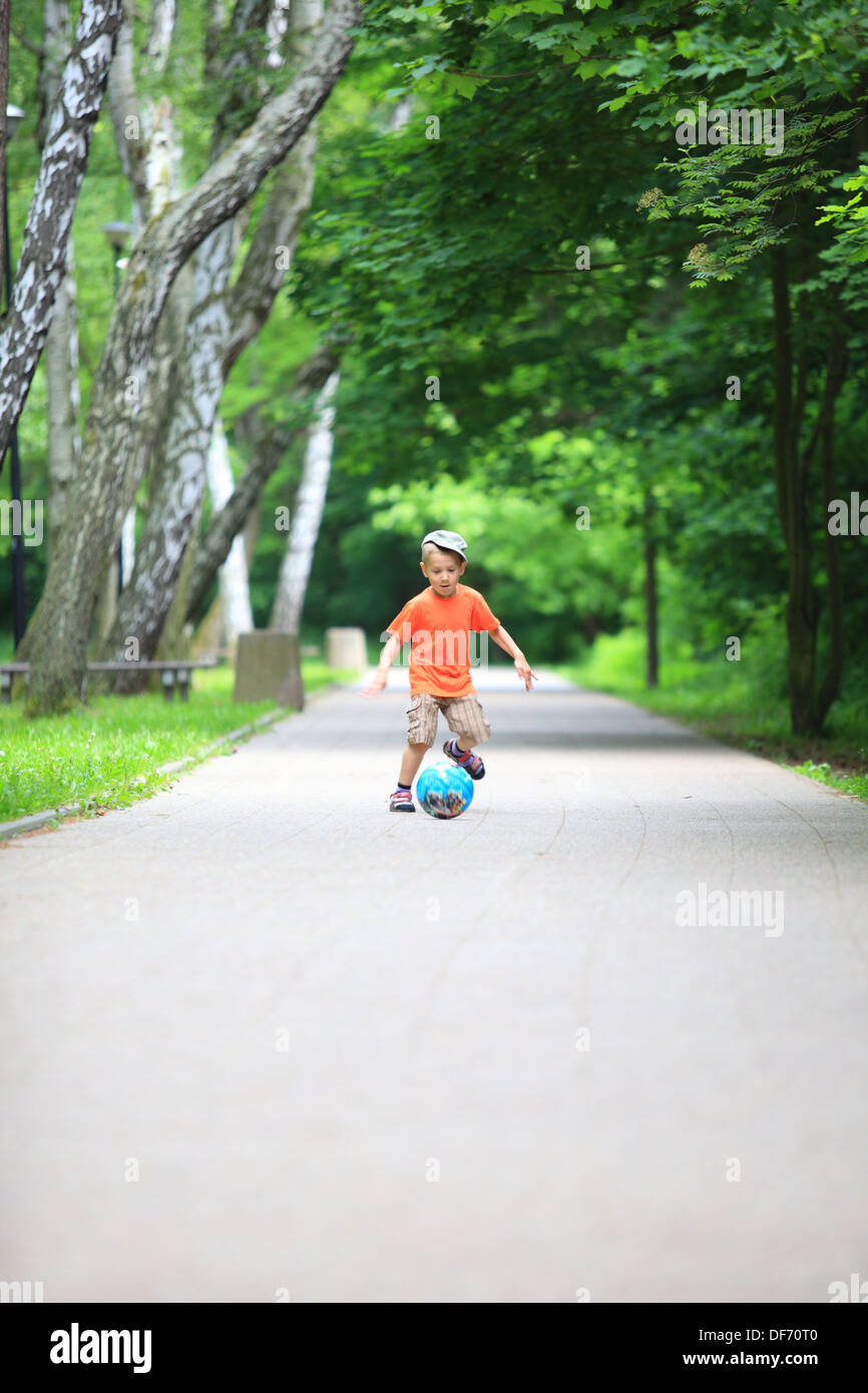 Boy young kid playing with ball kicks running towards ball in park ...