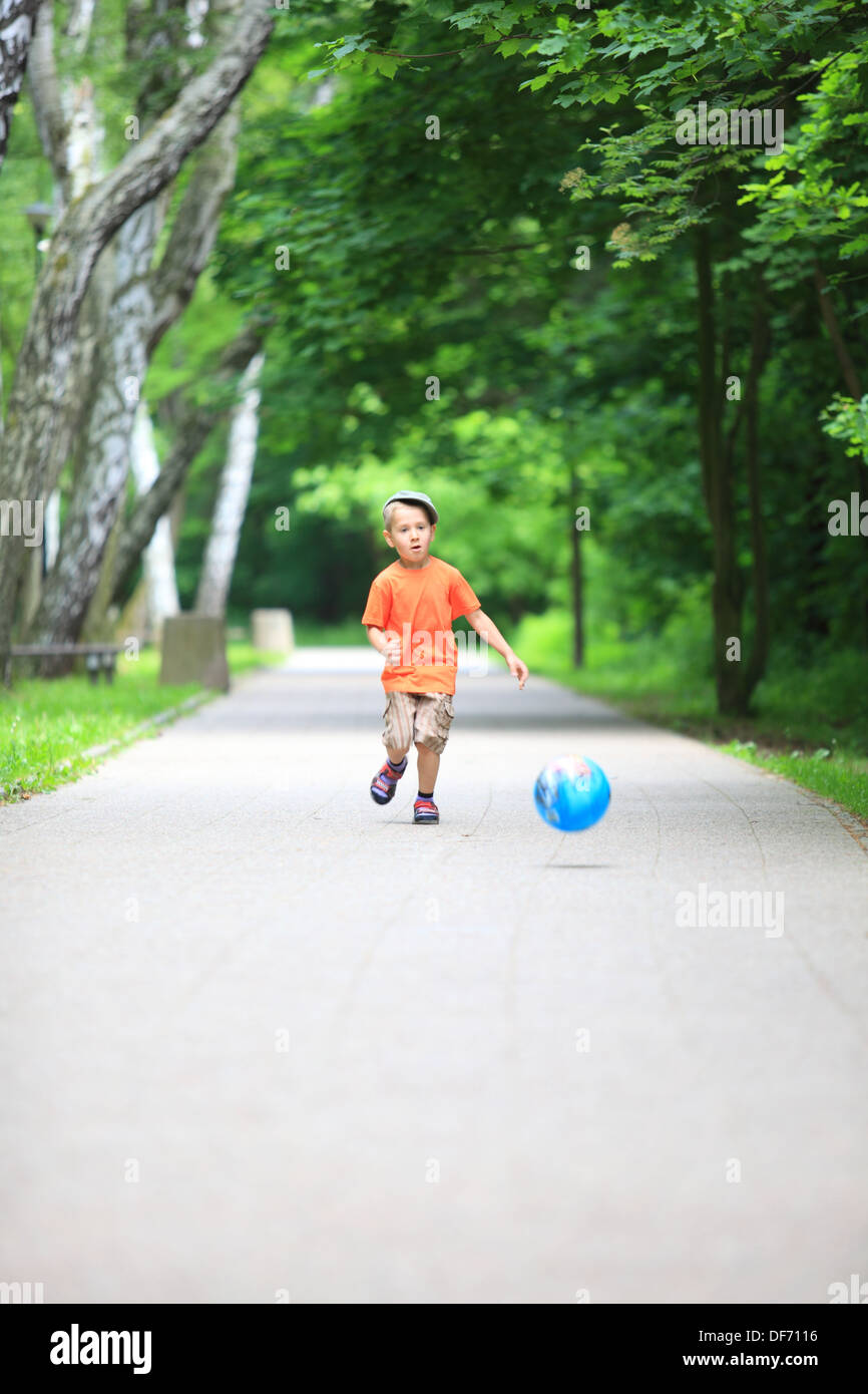 Boy young kid playing with ball kicks running towards ball in park ...