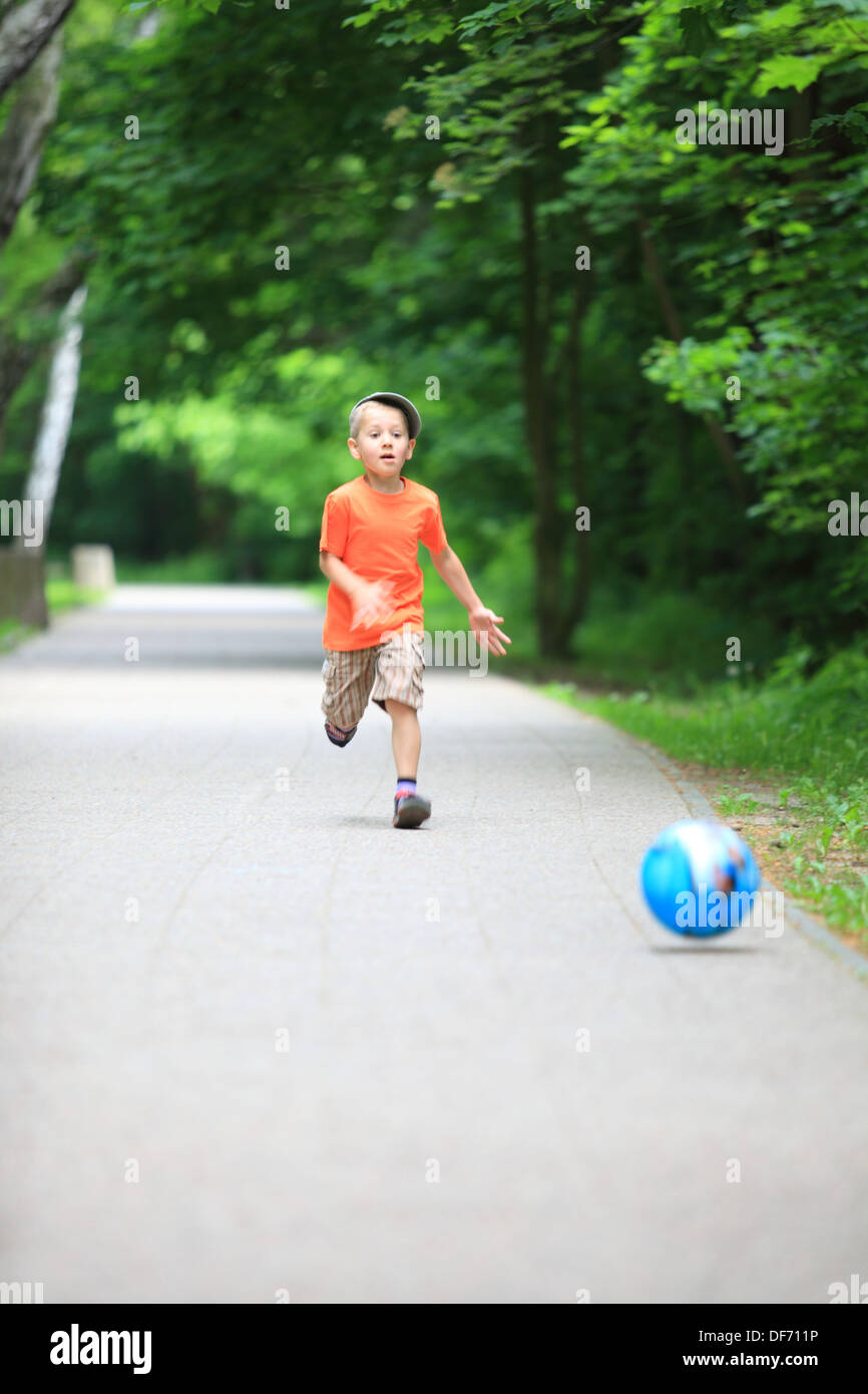 Boy young kid playing with ball kicks running towards ball in park ...
