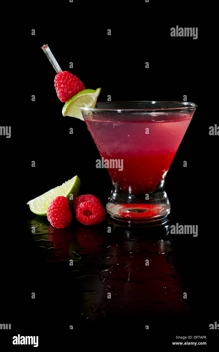 raspberry cocktail isolated on a black background garnished with a lime ...