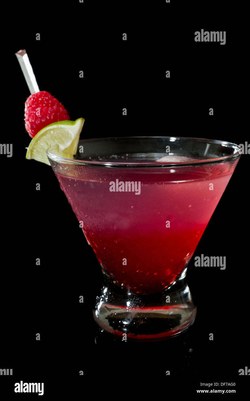 raspberry cocktail isolated on a black background garnished with a lime ...