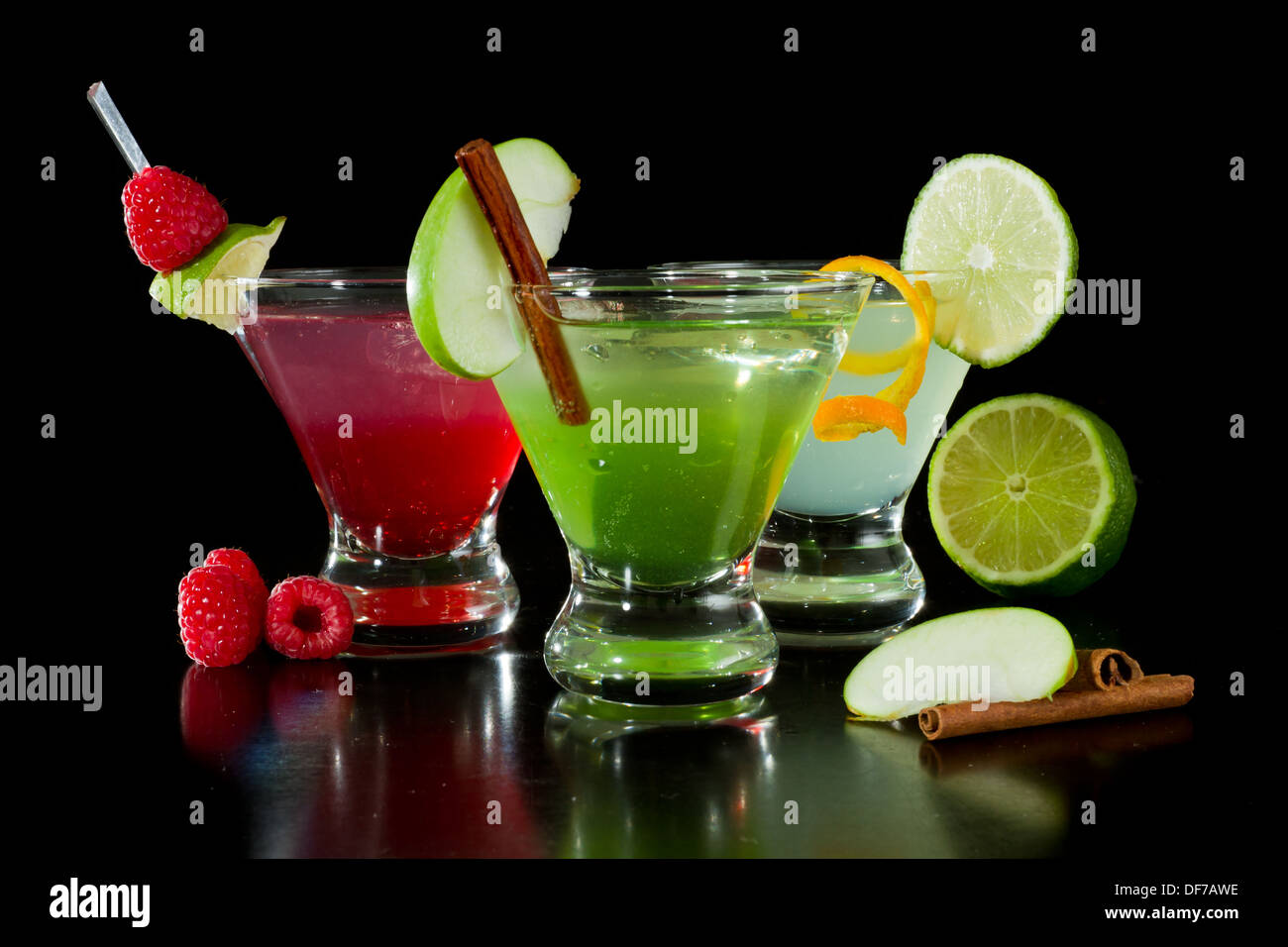 three bright martinis garnished with fresh fruit isolated on a black ...