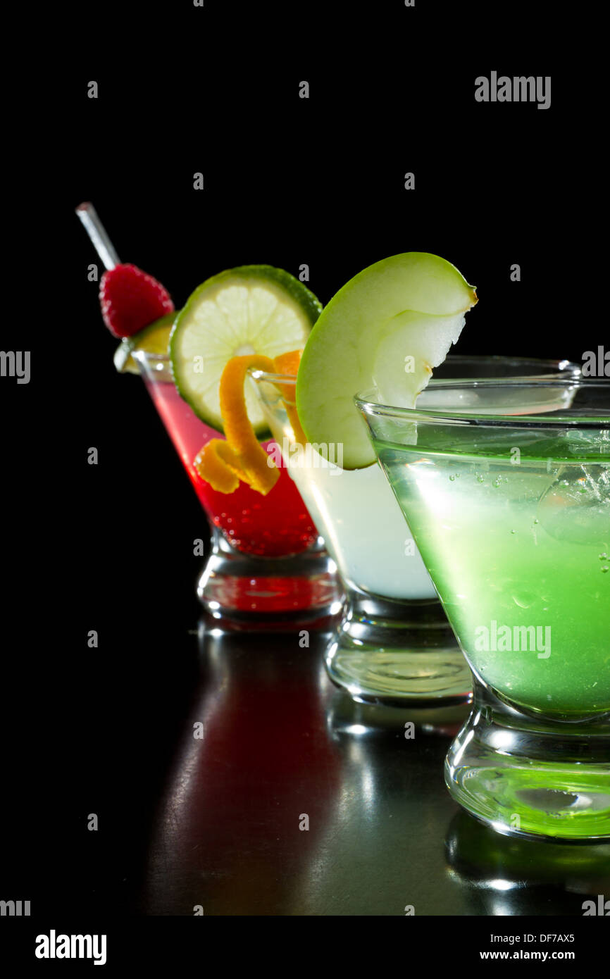 three bright martinis garnished with fresh fruit isolated on a black ...