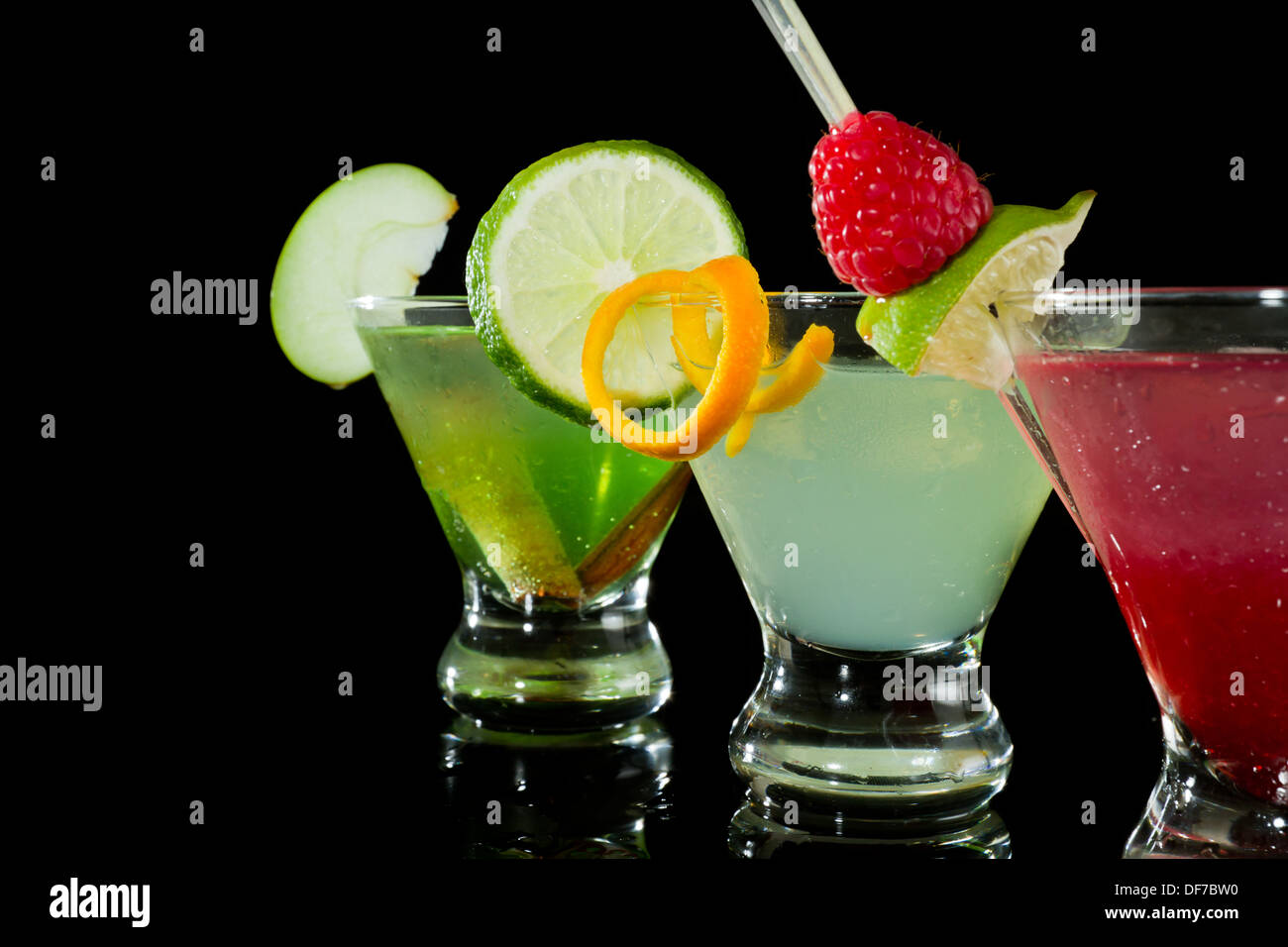 three bright martinis garnished with fresh fruit isolated on a black ...