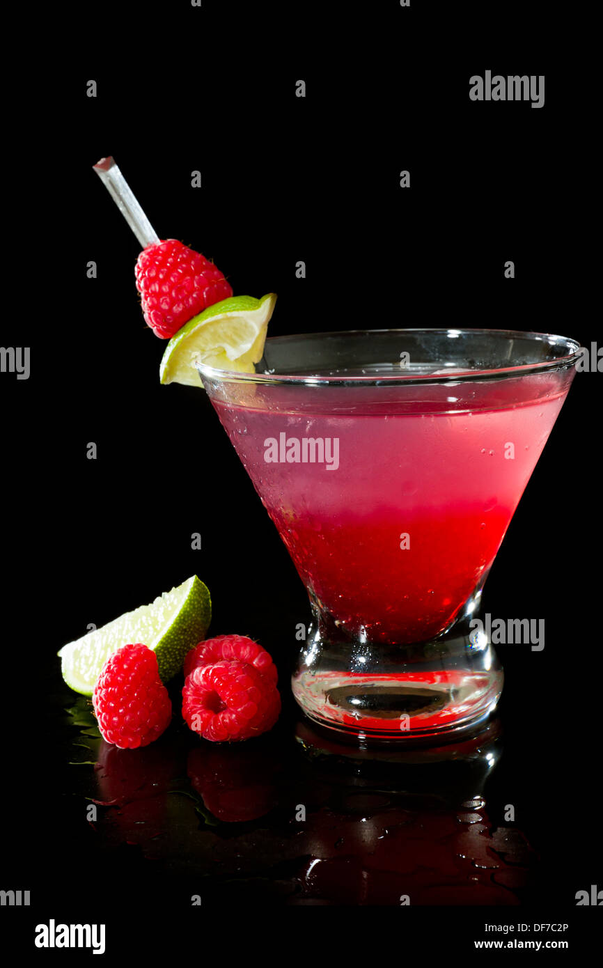 raspberry cocktail isolated on a black background garnished with a lime ...