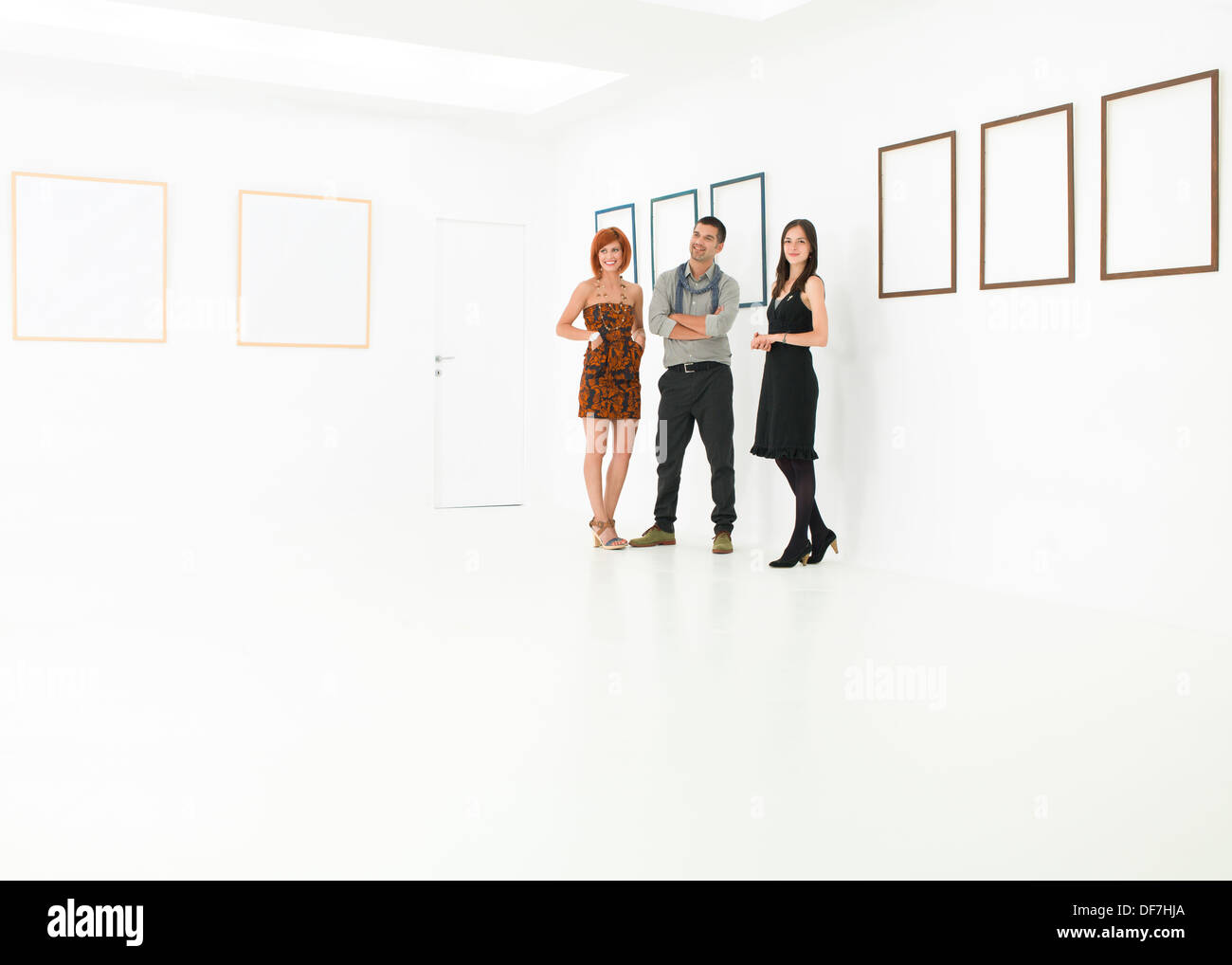 group of three people standing in a room with empty frames on walls ...
