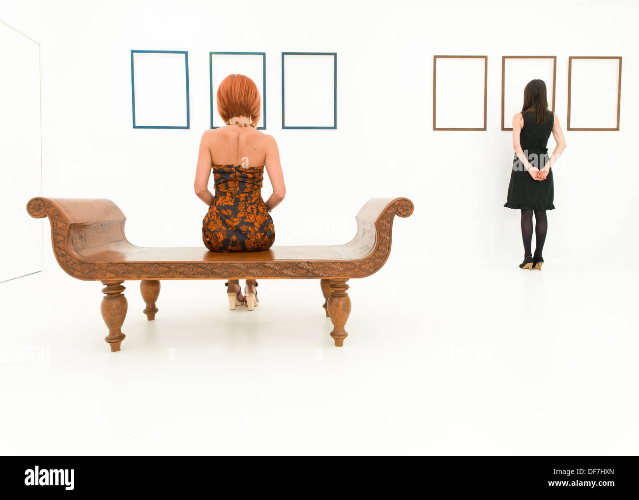 rear view of two women in a white room looking at empty frames ...