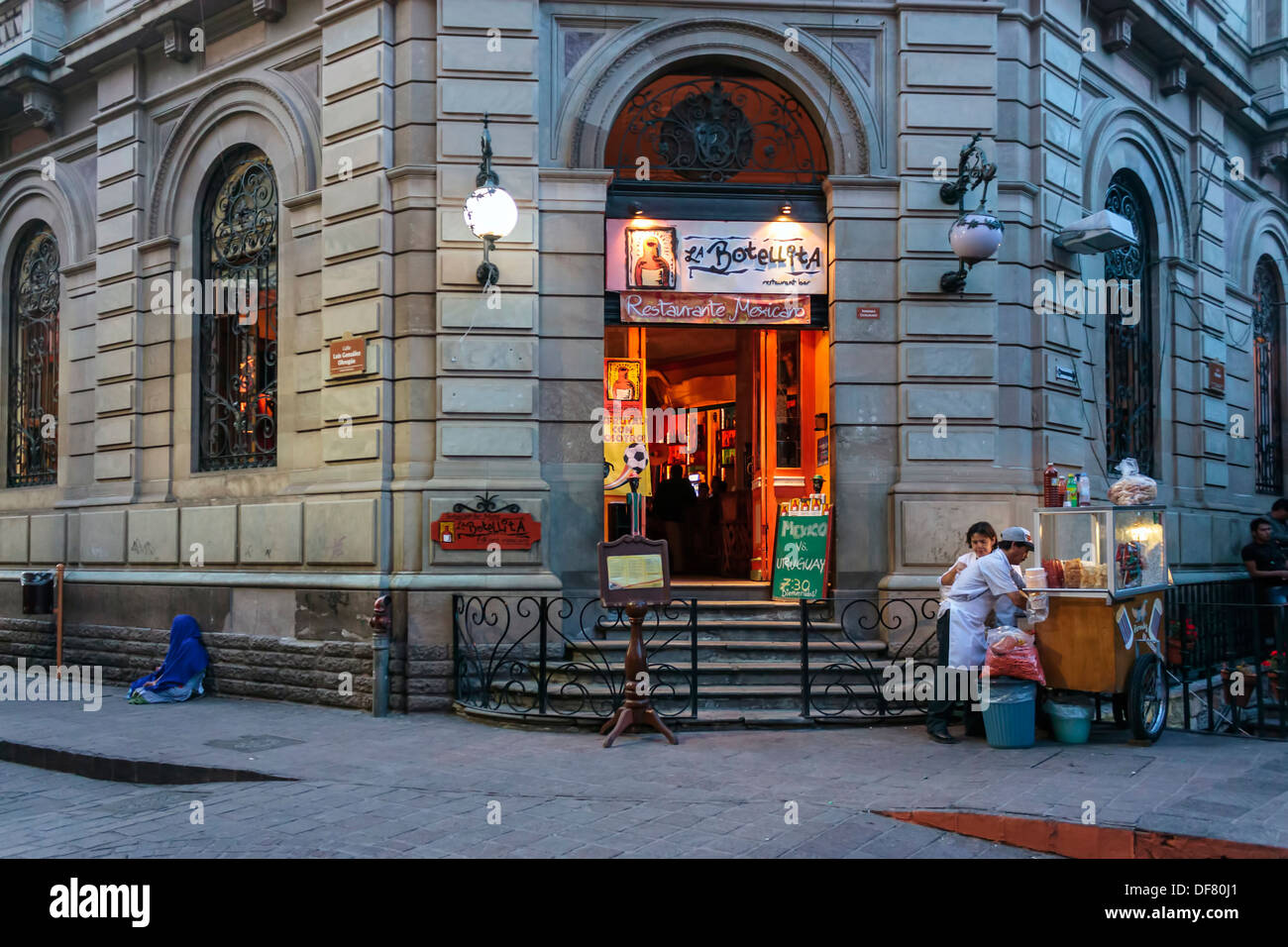 Picturesque shop, street food vendor and beggar woman on street corner ...
