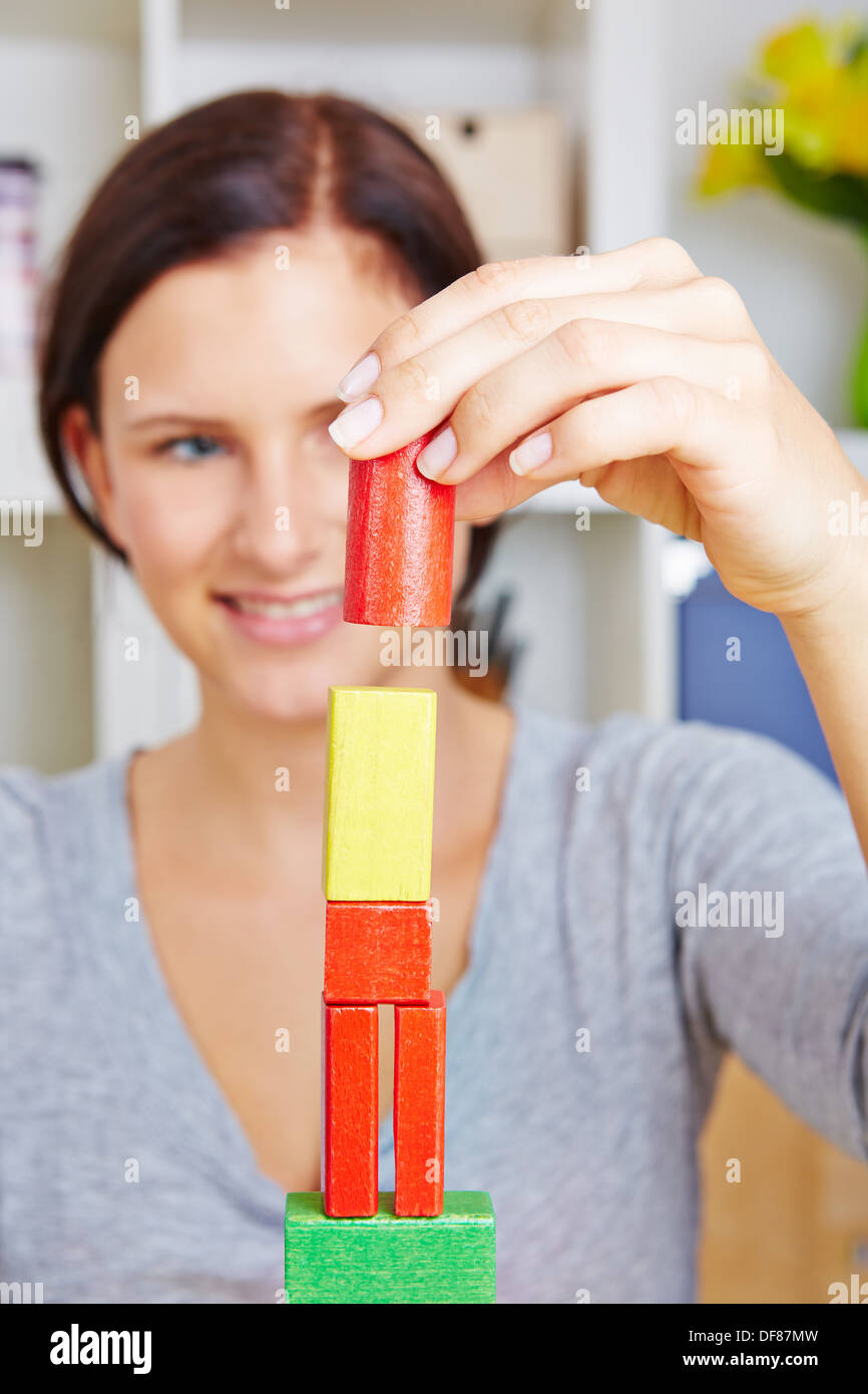 Young smiling woman building a tower with colorful building blocks ...